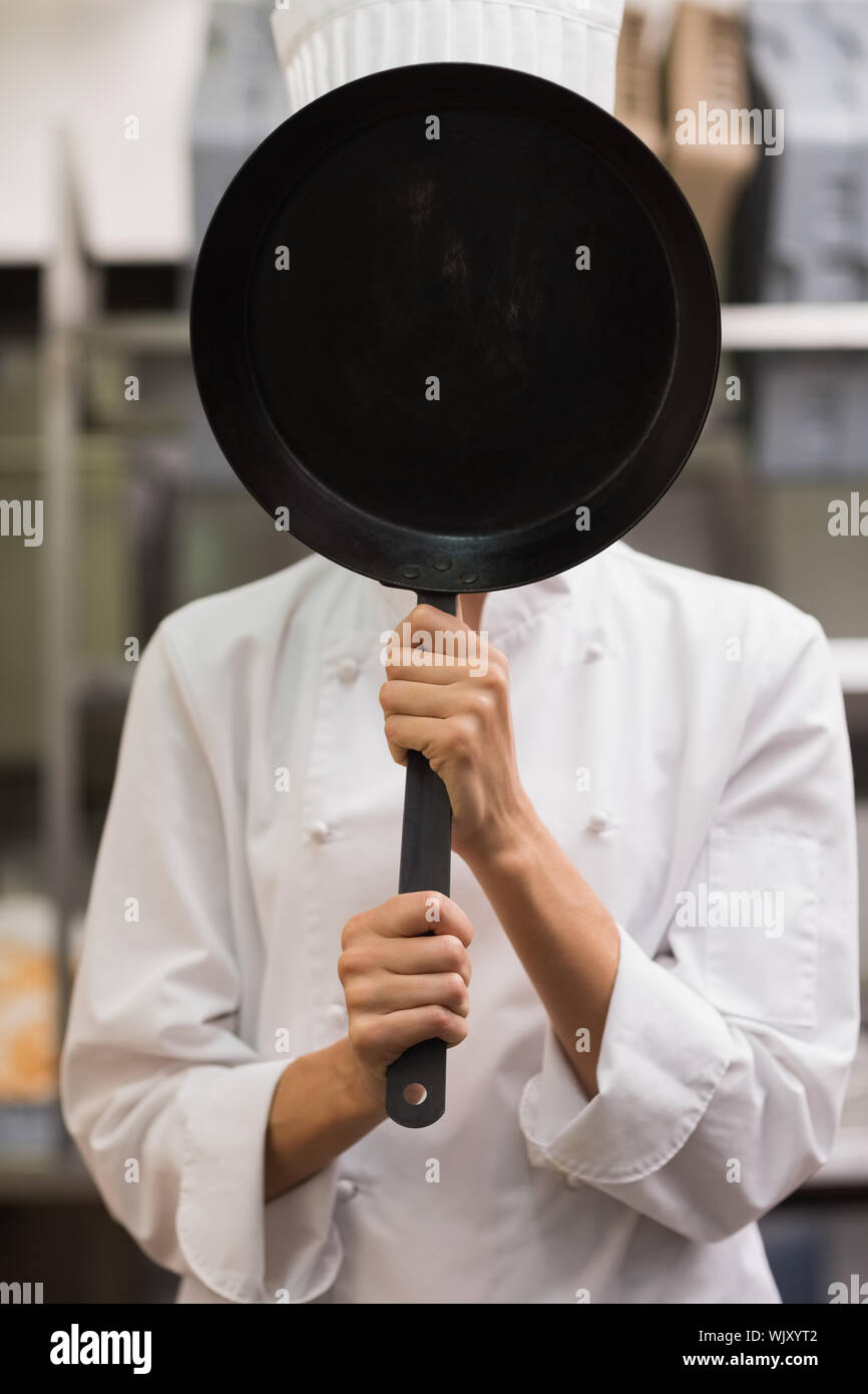 Chef standing covering face with frying pan in a commercial kitchen ...