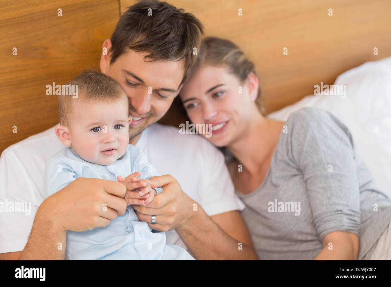 Happy parents relaxing on bed with their baby son at home in bedroom ...