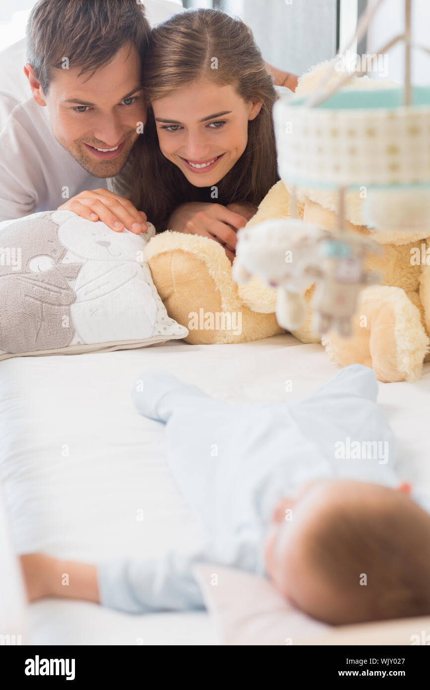Happy parents watching over baby son sleeping in crib at home in ...