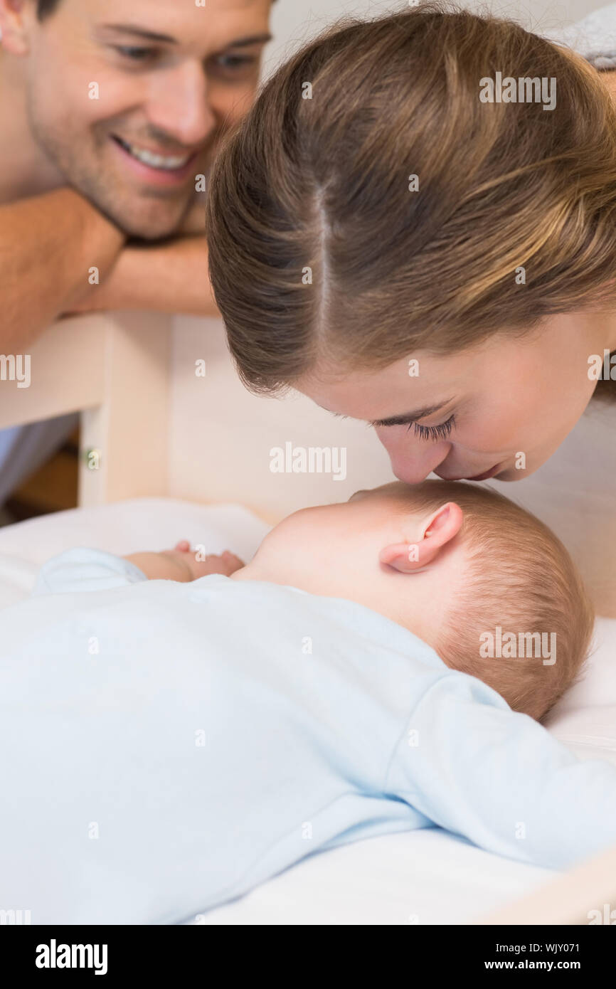 Happy parents watching over baby son sleeping in crib at home in ...