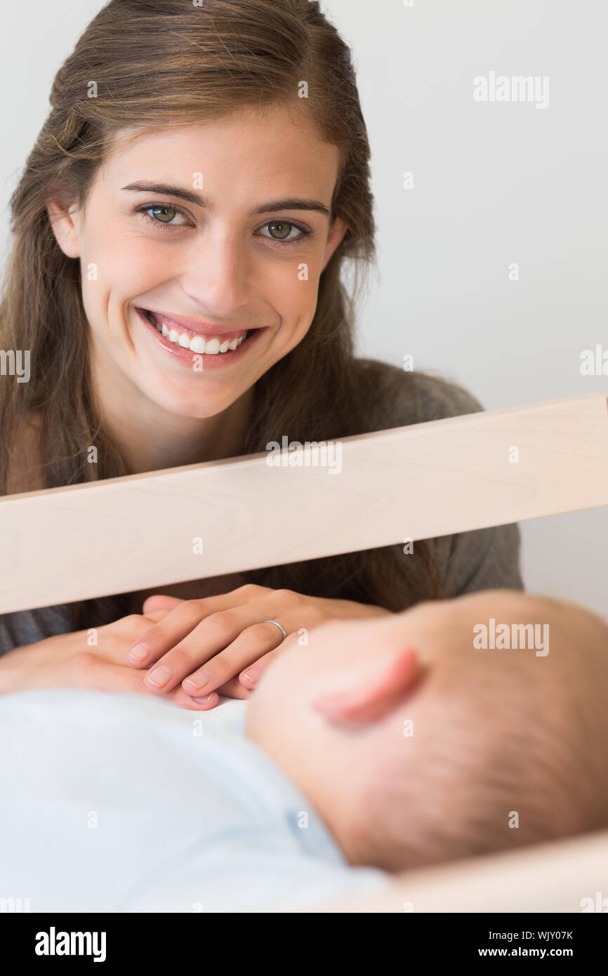 Happy mother watching over baby son sleeping in crib at home in bedroom ...