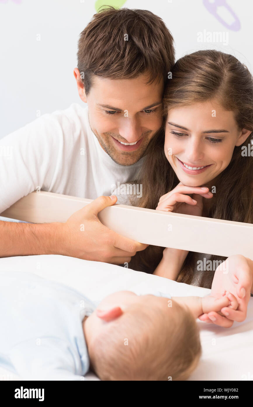 Happy parents watching over baby son sleeping in crib at home in ...