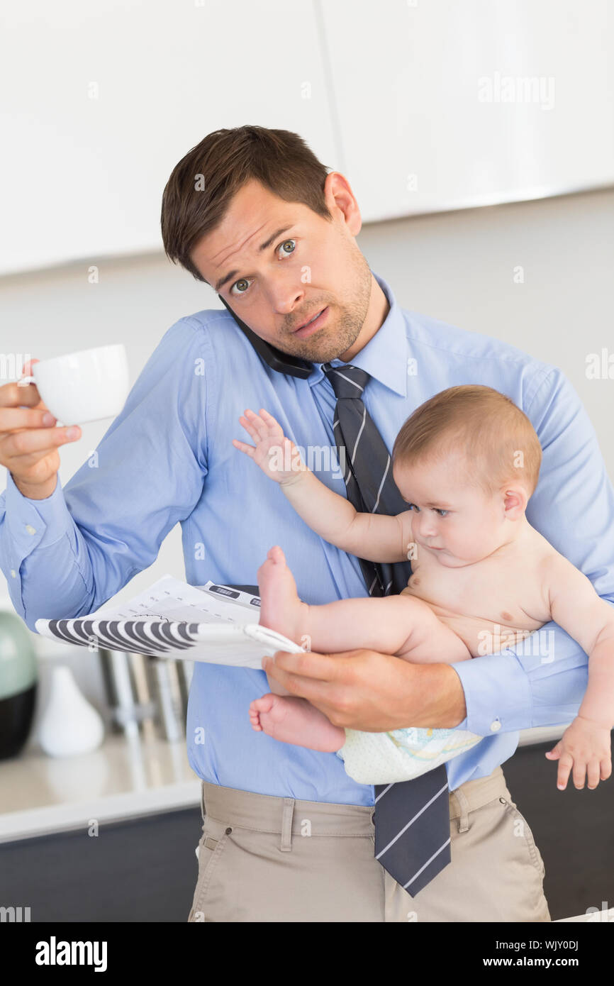 Busy father holding his baby son before work at home in the kitchen ...