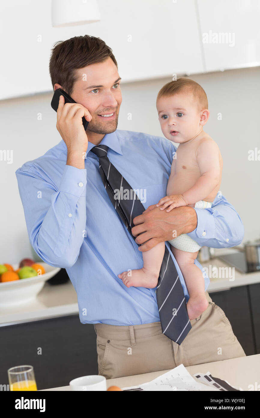 Busy father holding his baby son before work at home in the kitchen ...