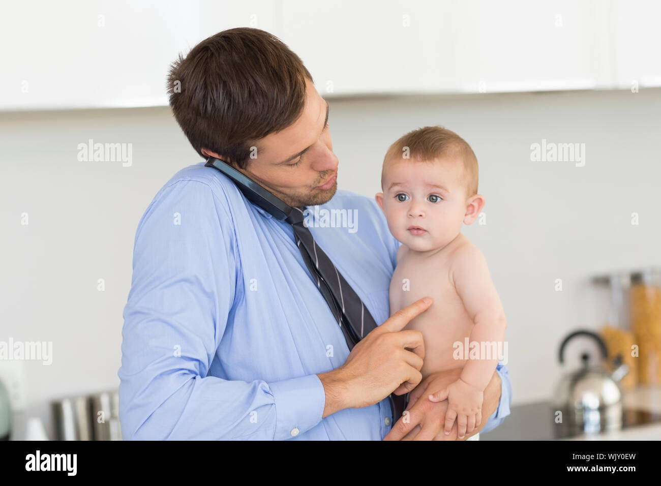 Busy father holding his baby son before work at home in the kitchen ...