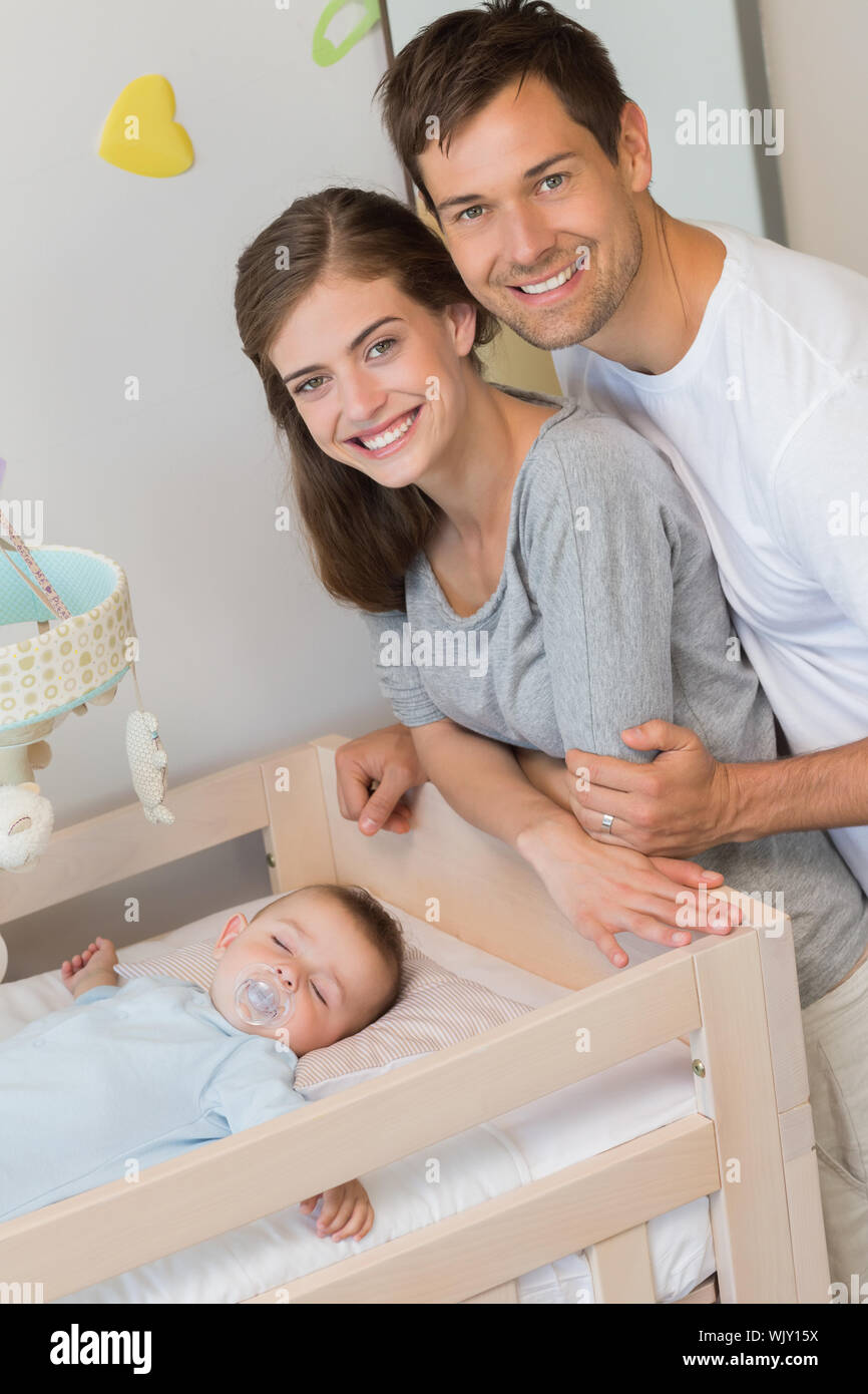 Happy parents watching over baby son in crib at home in bedroom Stock ...