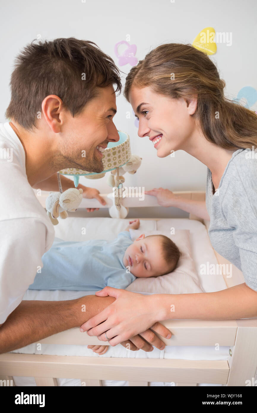 Happy parents watching over baby son in crib at home in bedroom Stock ...