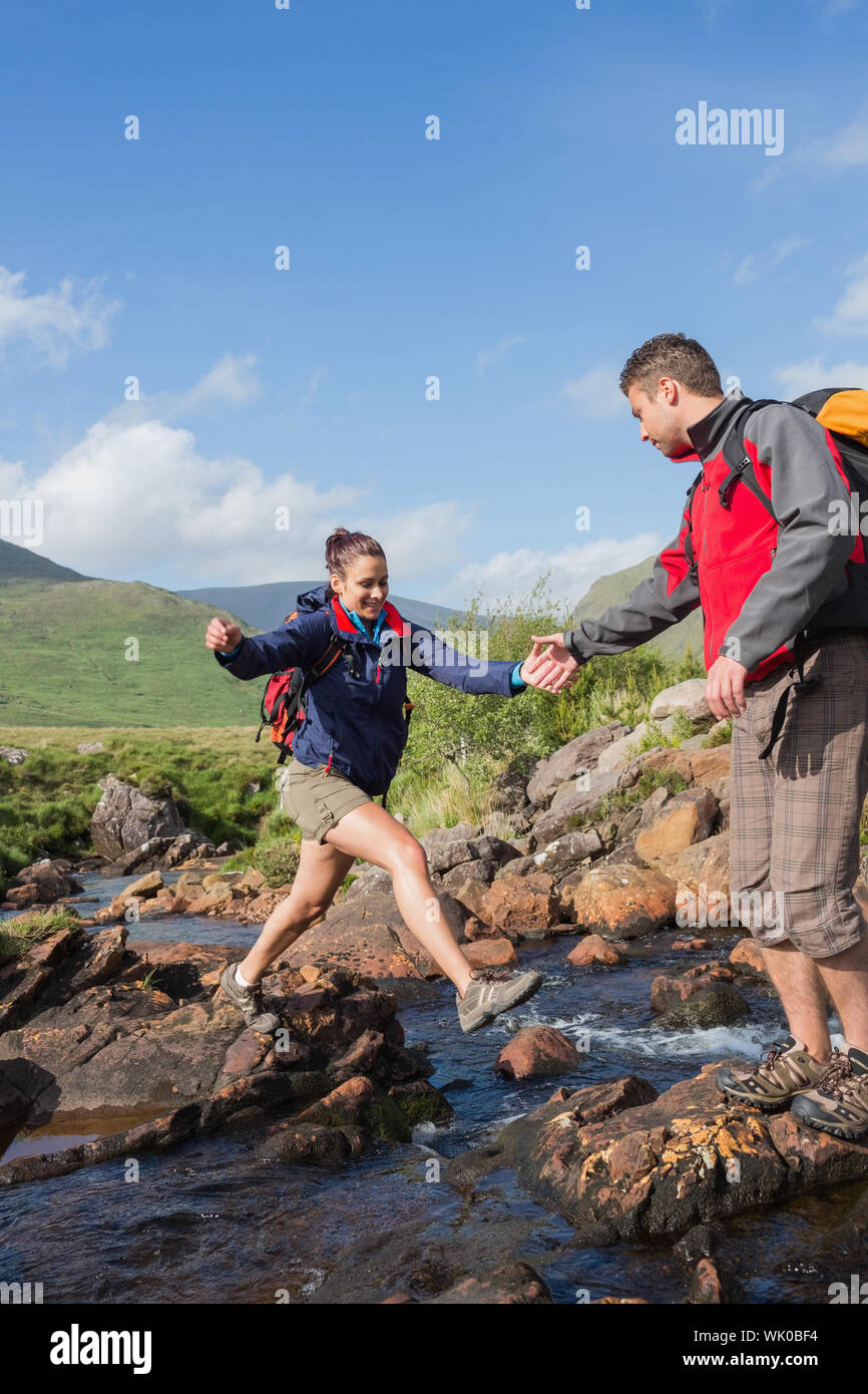 Man helping his girlfriend to cross a stream Stock Photo - Alamy
