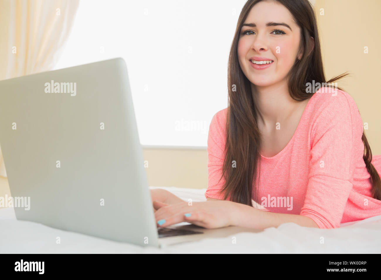 Pretty Young Girl Looking At Camera Using A Laptop Lying On A Bed Stock