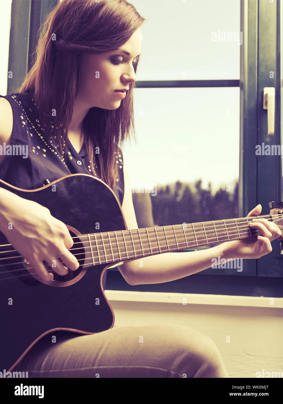 Photo of a woman playing an acoustic guitar by a window. Heavily ...