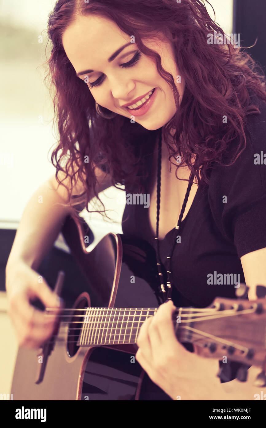 Photo of a woman playing an acoustic guitar by a window. Heavily ...