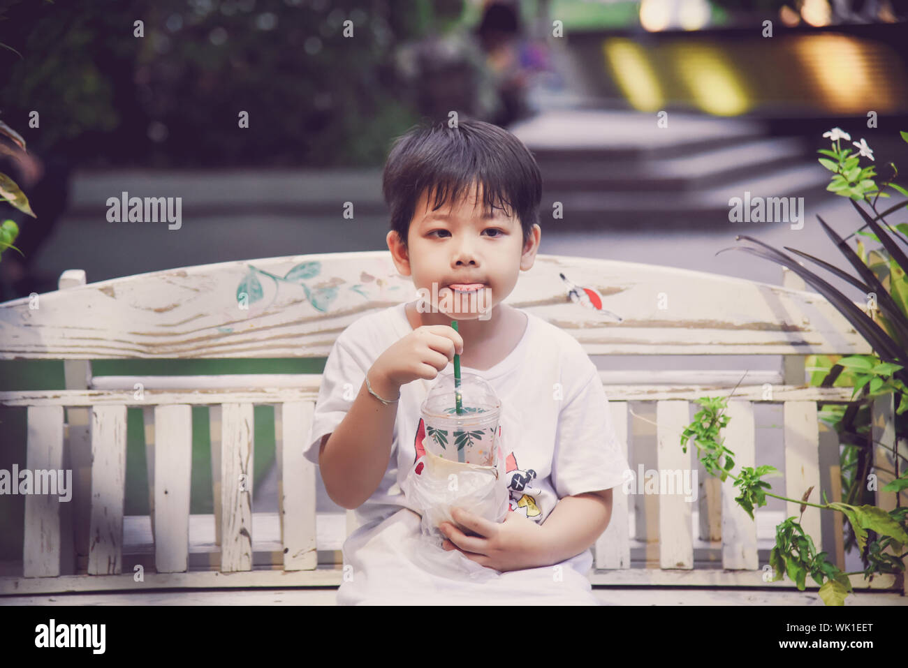 Full Length Of Boy Having Drink While Sitting On Bench Stock Photo - Alamy