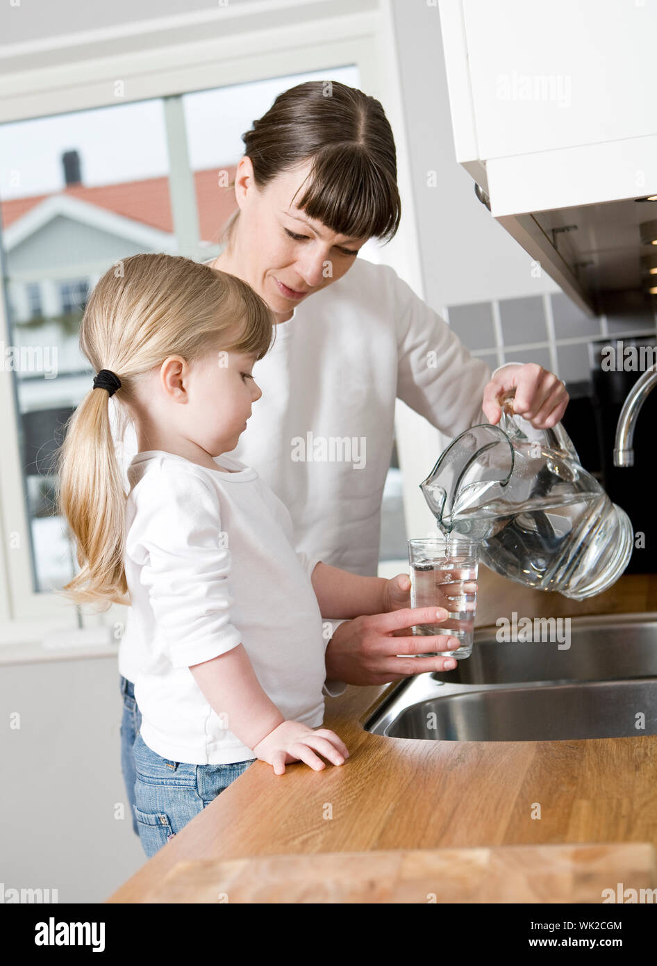 Small Girl in the kitchen with her mother drinking water Stock Photo ...
