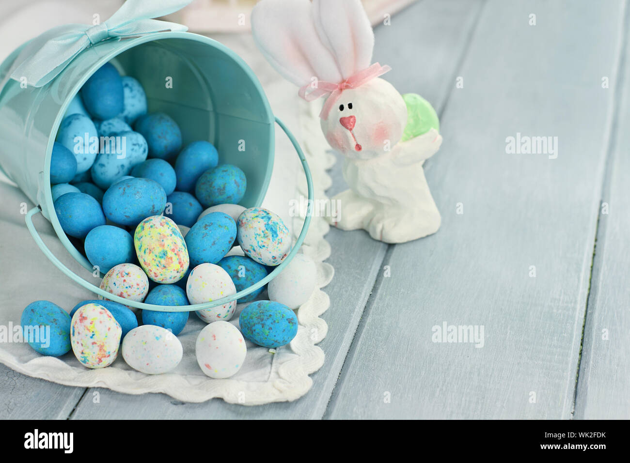A blue tin bucket tipped over, spilling Easter candy eggs onto a table ...