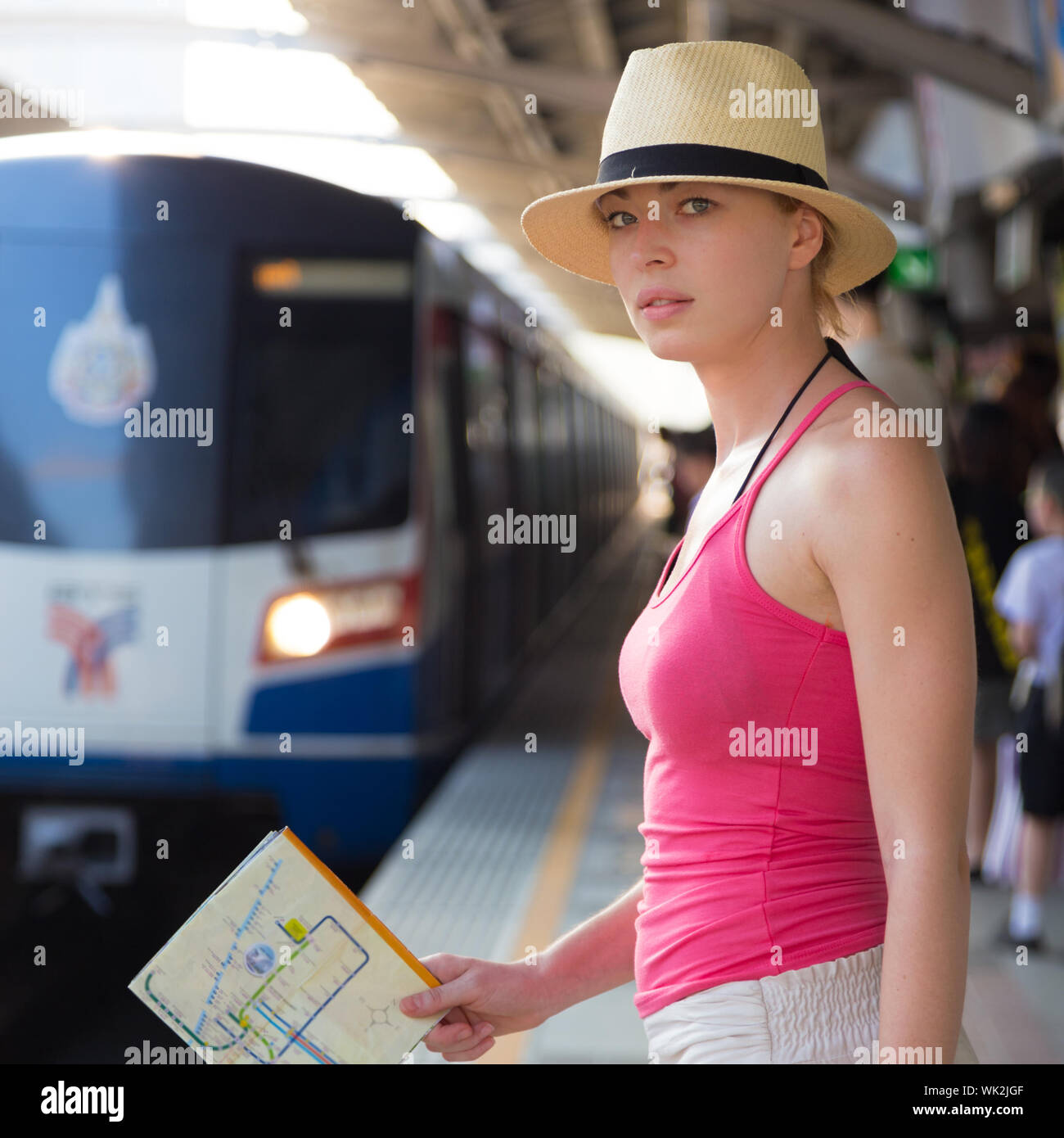 Young woman with a map in her hand waiting on the platform of a railway ...
