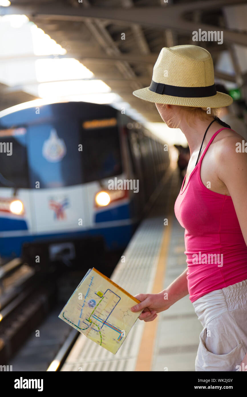Young woman with a map in her hand waiting on the platform of a railway ...
