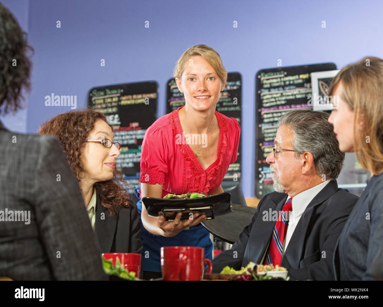 Pretty young server bringing food to group of business people Stock ...