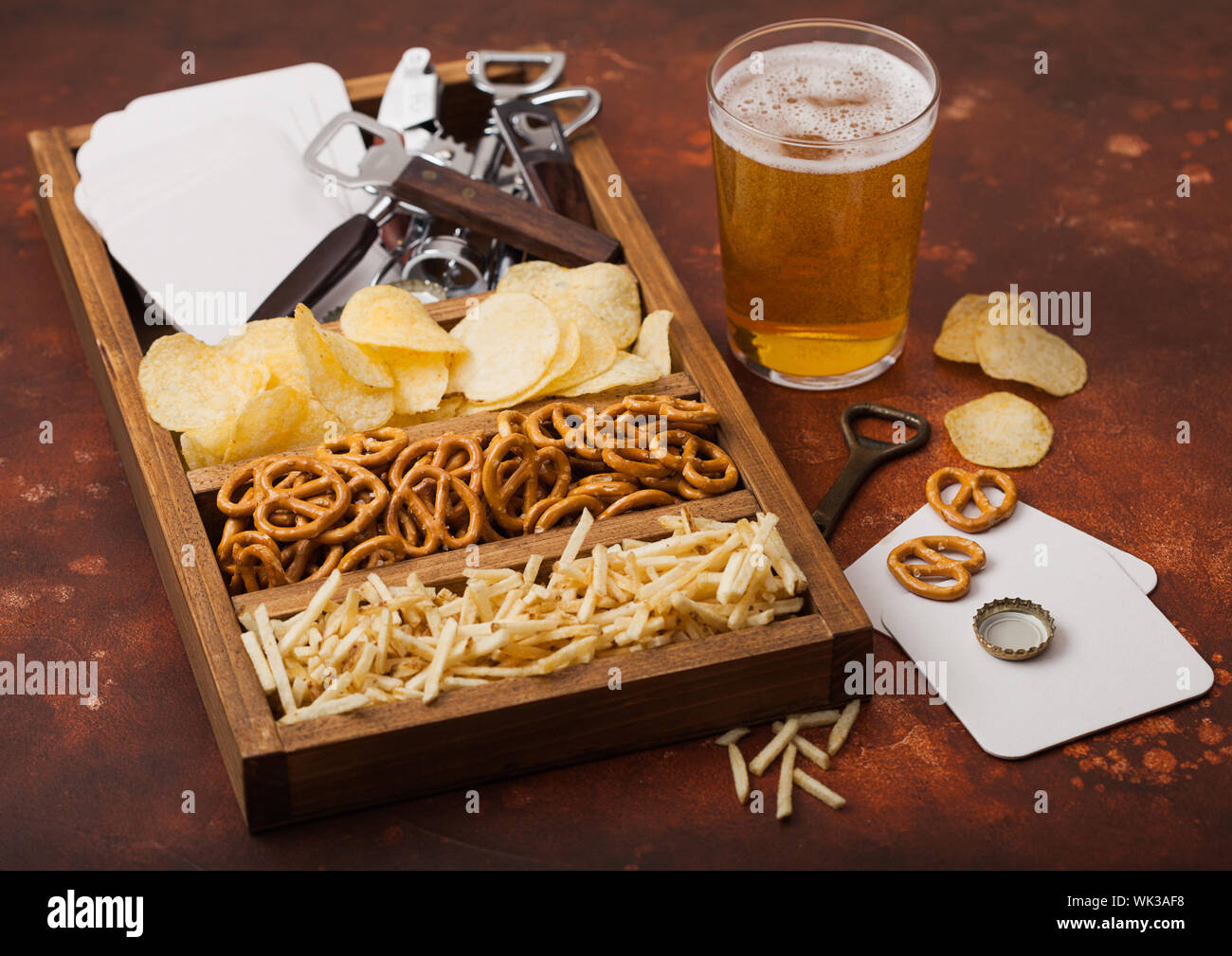 Glass of craft lager beer and opener with box of snacks on brown ...