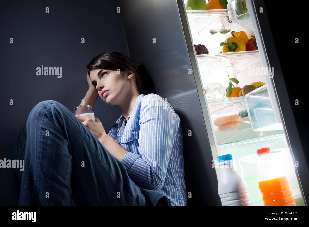 Sleepless sad woman sitting on kitchen floor having a glass of milk ...
