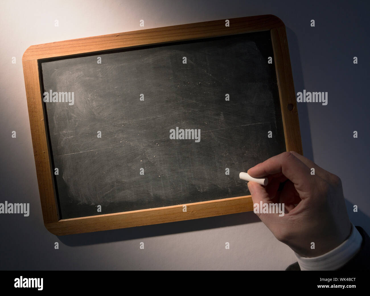Hand holding chalk over chalkboard on desk Stock Photo - Alamy
