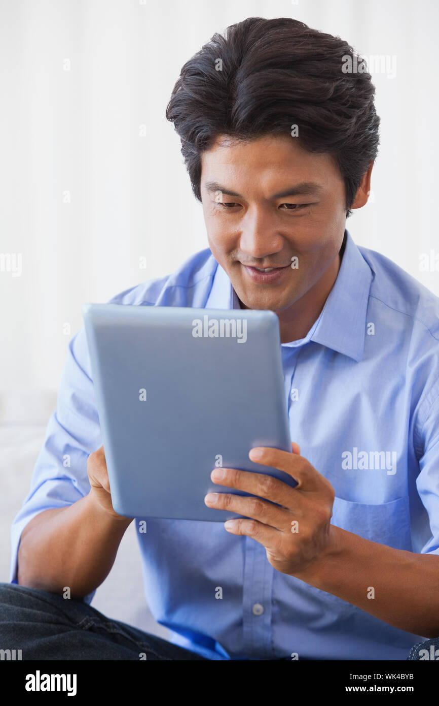 Happy man sitting on couch using tablet at home in the living room ...