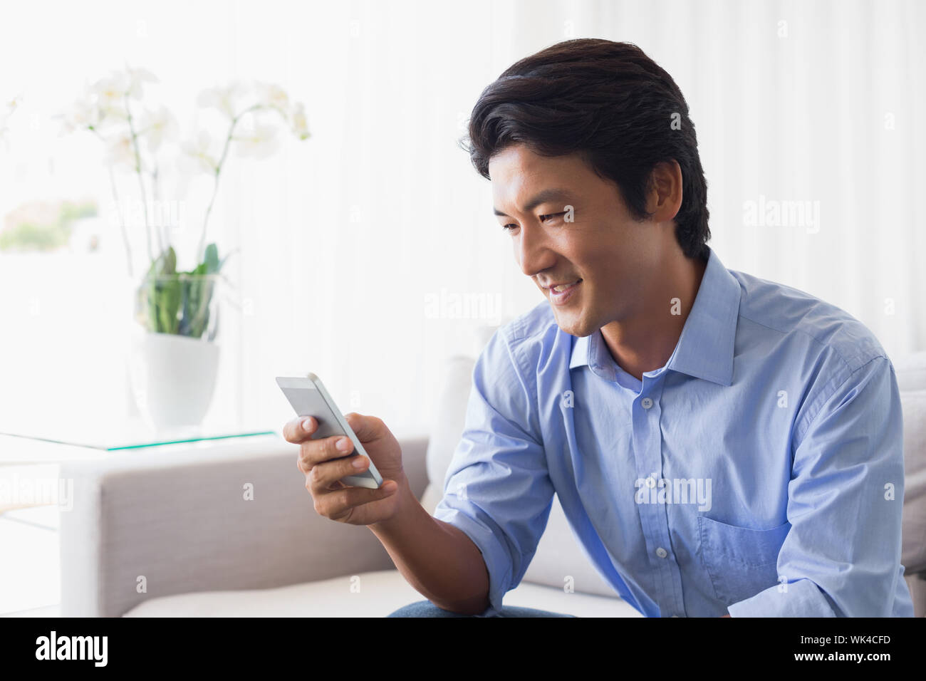 Happy man sitting on couch texting on phone at home in the living room ...