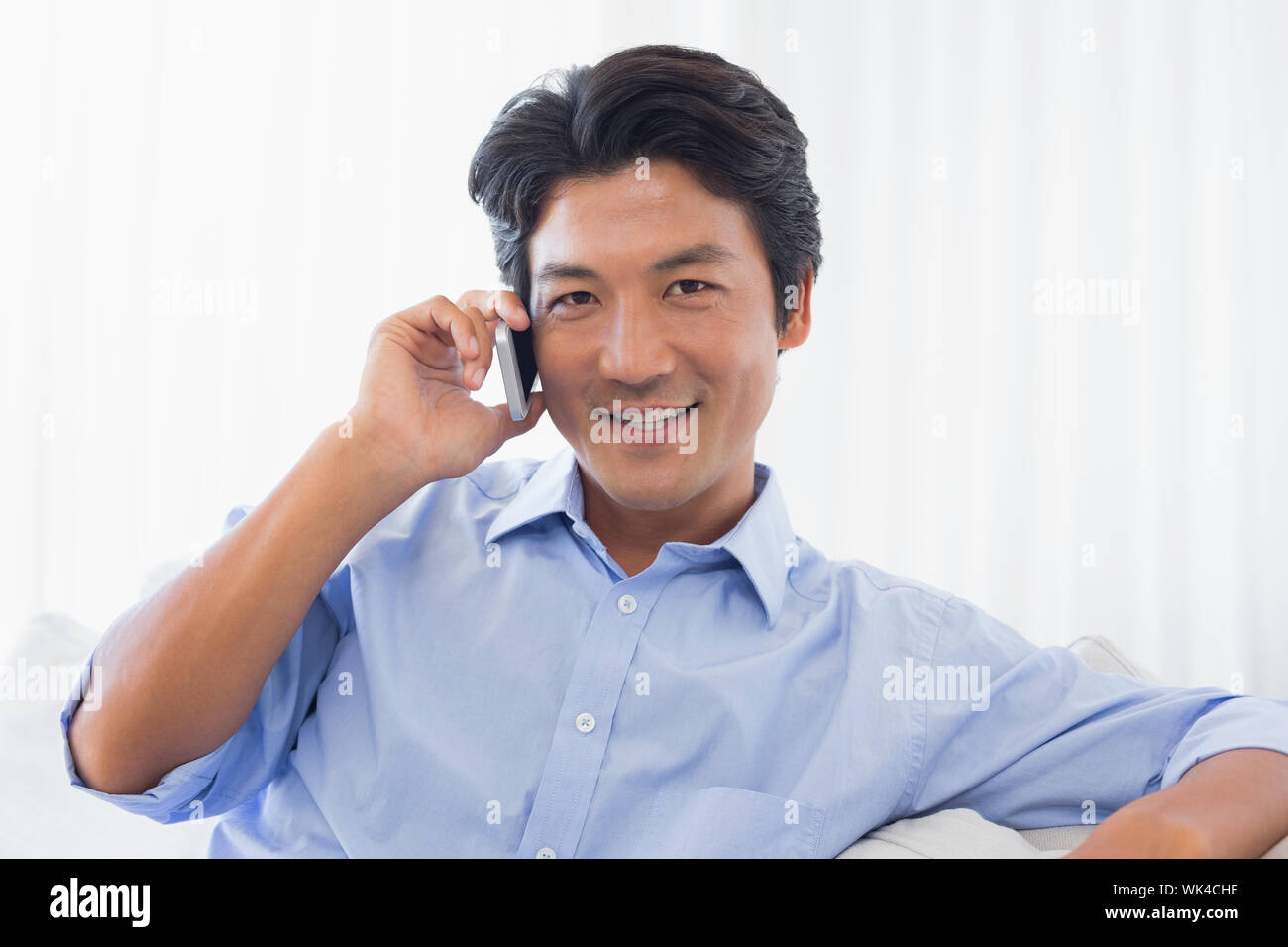 Happy man relaxing on couch talking on phone at home in the living room ...