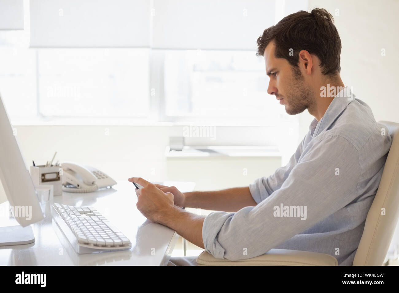 Casual businessman sending a text at his desk in his office Stock Photo ...