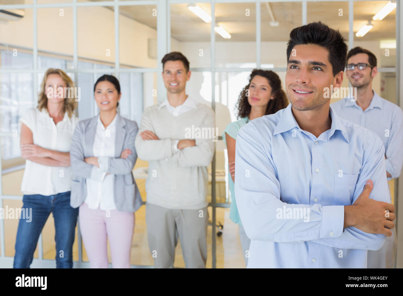 Casual boss smiling with arms crossed in front of business team in the ...