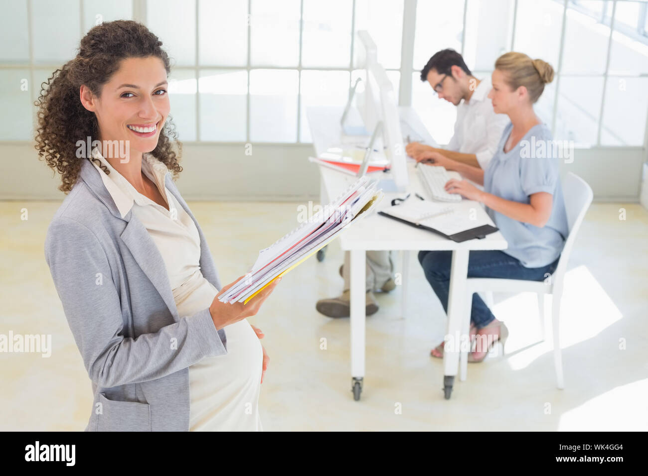 Pregnant businesswoman smiling at camera with team behind her in the ...