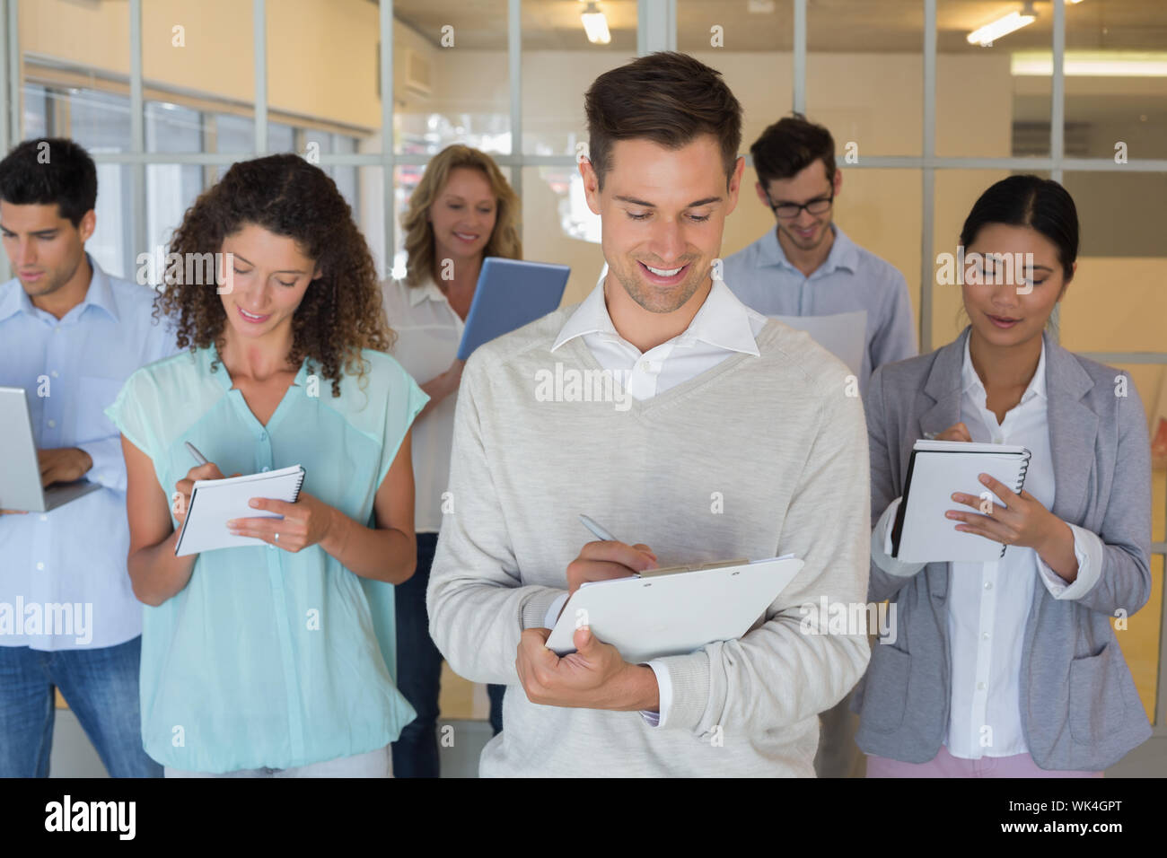 Casual boss standing in front of his team all taking notes in the ...
