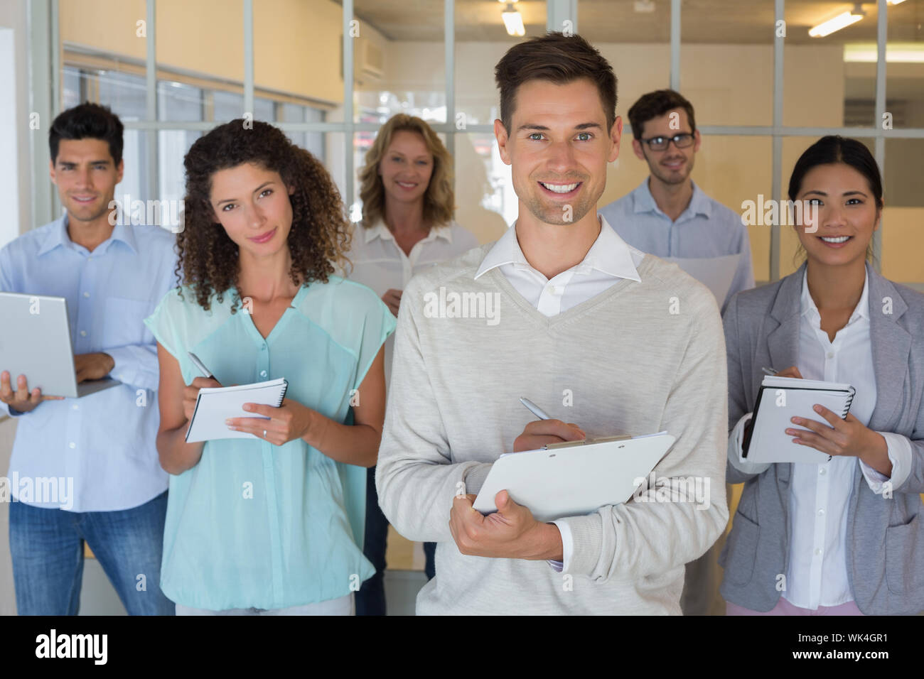 Casual boss standing in front of his team all taking notes in the ...