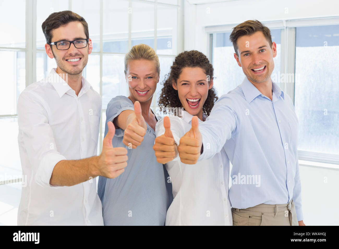 Casual business team smiling at camera and showing thumbs up in the ...
