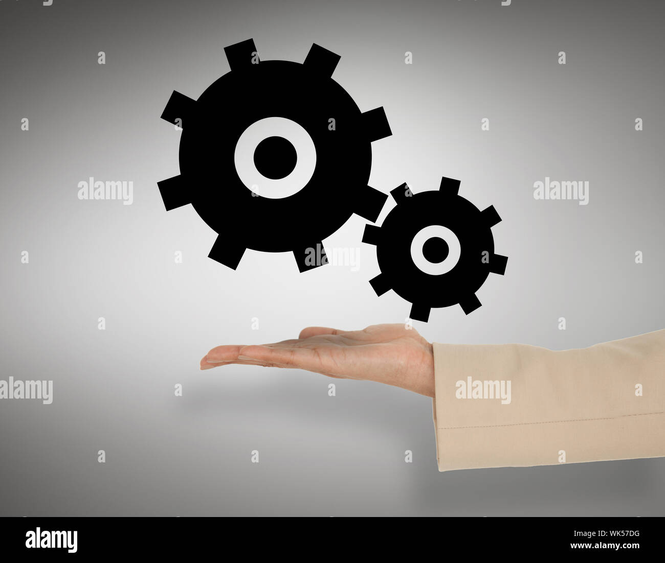 Female hand presenting cogs and wheels against grey vignette Stock ...