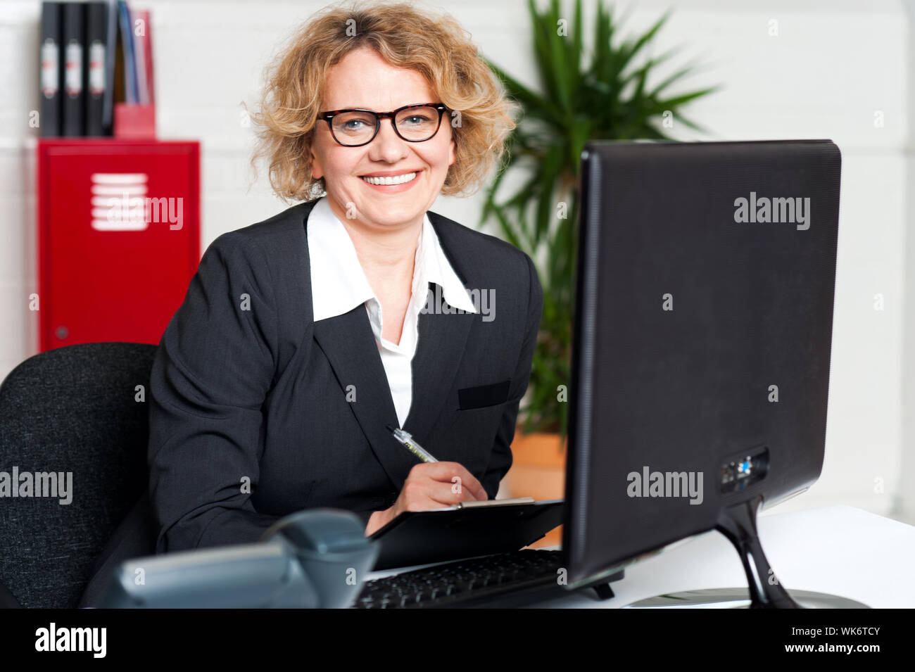 Female executive writing notes on clipboard looking at you Stock Photo ...