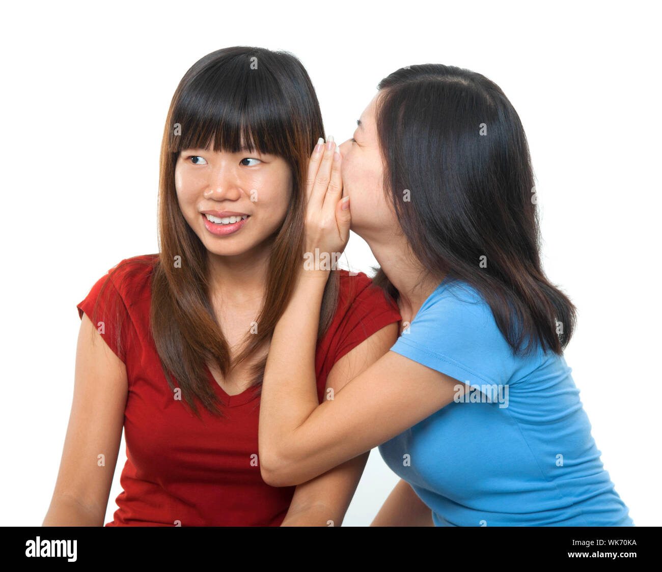 Two young Asian girls sharing secrets, isolated on white background ...