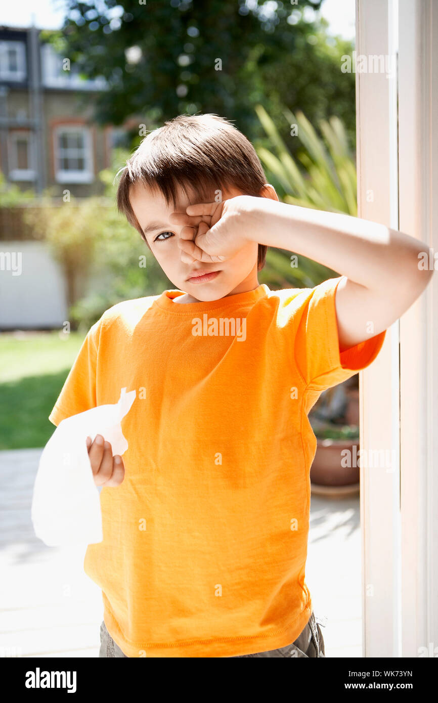 Portrait of young boy with tissue paper rubbing eye in backyard Stock ...