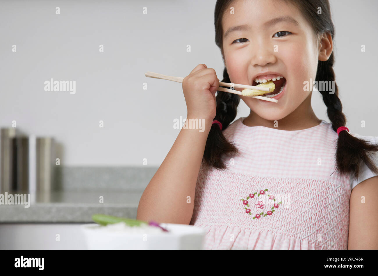 Portrait of a little girl with pigtails eating baby corn with ...