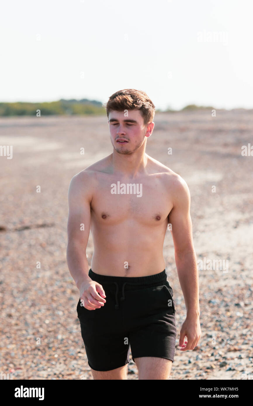 Young caucasian shirtless man wearing swimwear walking on a beach on a ...