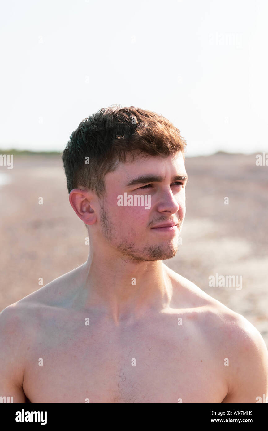 Young caucasian shirtless man wearing swimwear walking on a beach on a ...