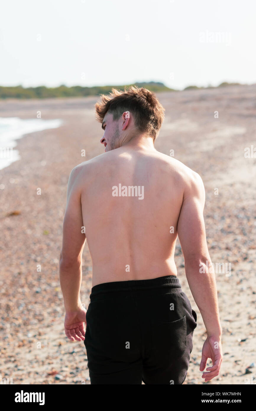 Young caucasian shirtless man wearing swimwear walking on a beach on a ...