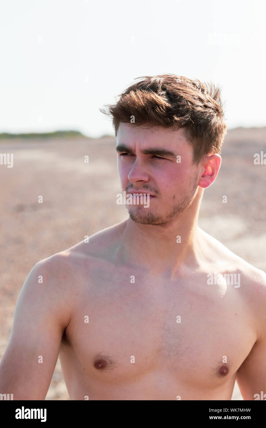 Young caucasian shirtless man wearing swimwear walking on a beach on a ...