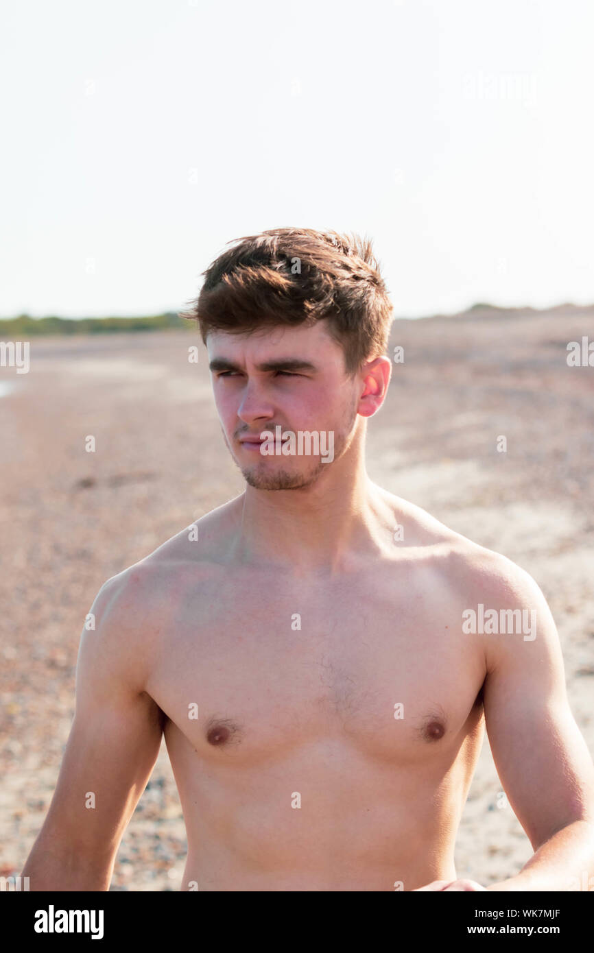 Young caucasian shirtless man wearing swimwear walking on a beach on a ...