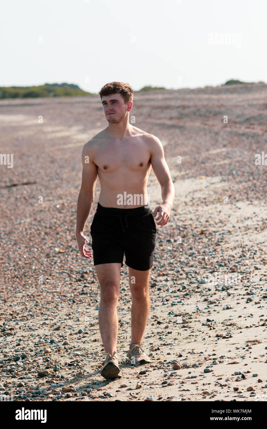 Young caucasian shirtless man wearing swimwear walking on a beach on a ...