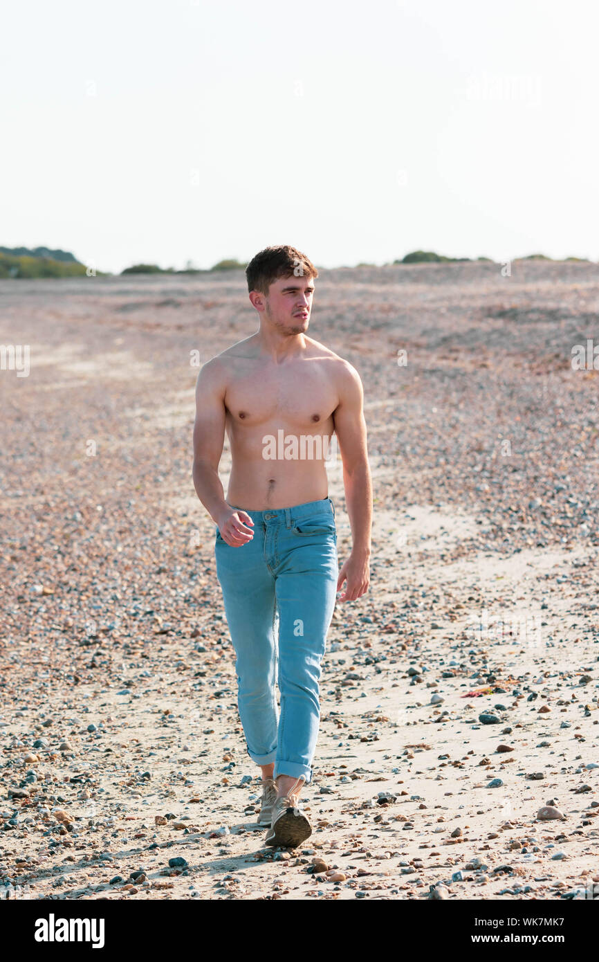 Young caucasian shirtless man wearing blue jeans walking on a beach on ...