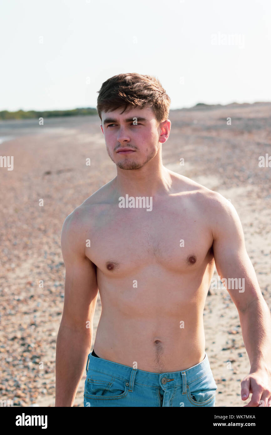 Young caucasian shirtless man wearing blue jeans walking on a beach on ...