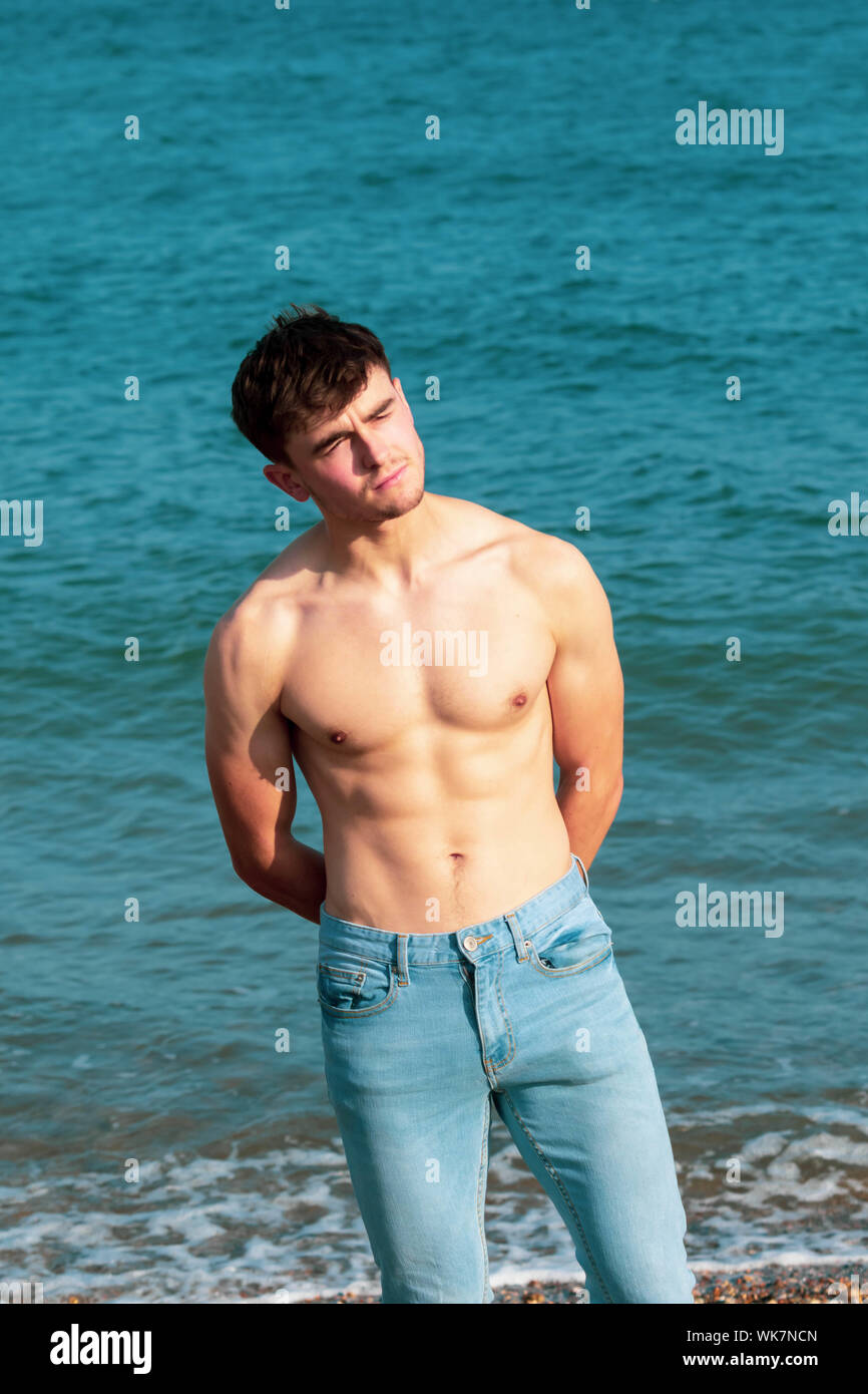 Young shirtless muscular caucasian man, posing on a beach on a warm ...