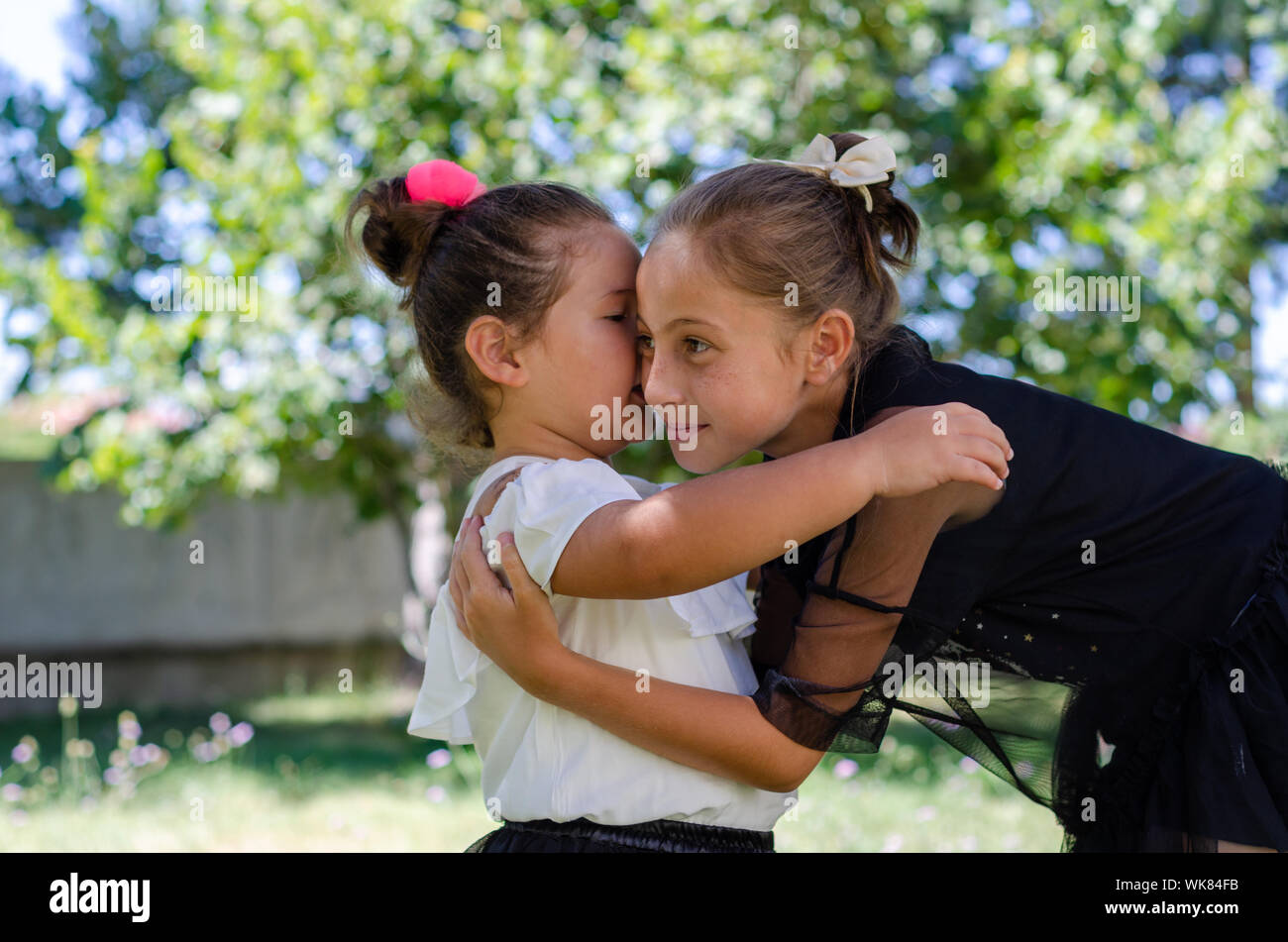 Two cute sisters are hugging each other outdoors and elder sister is ...