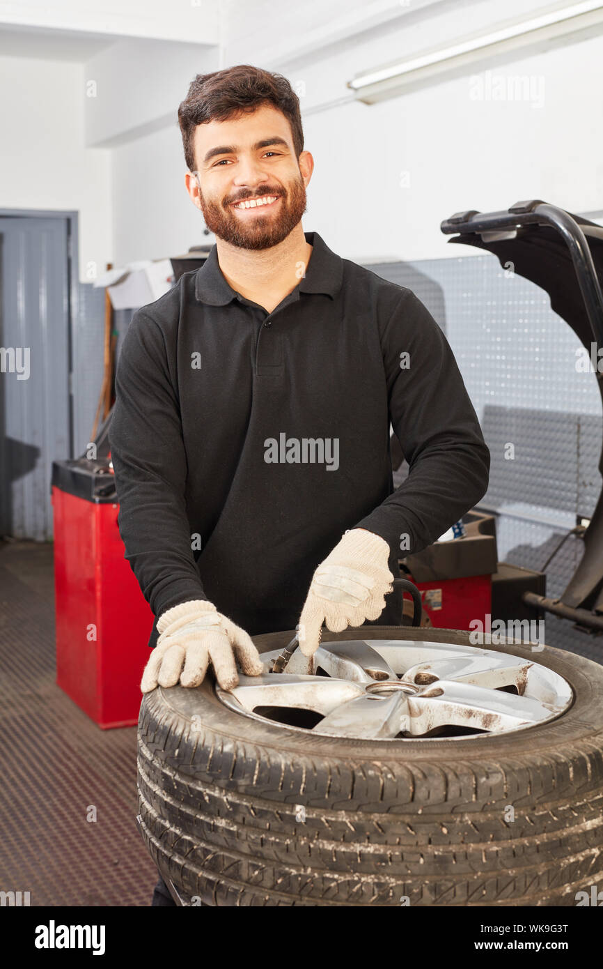 Smiling car mechanic with rim and tires at tire fitting in workshop ...