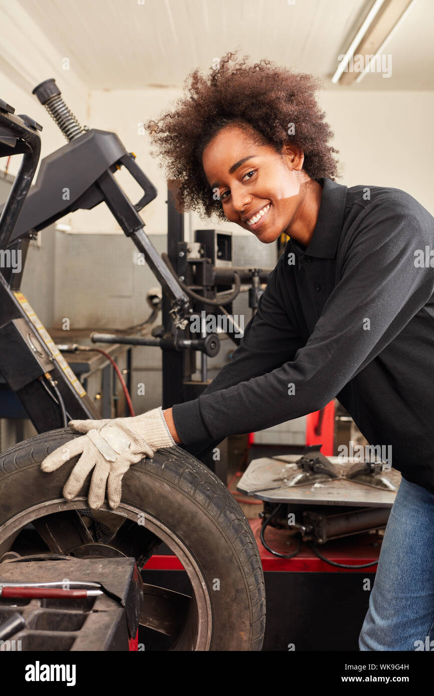 Young African woman as a mechanic apprentice with car tires in the car ...